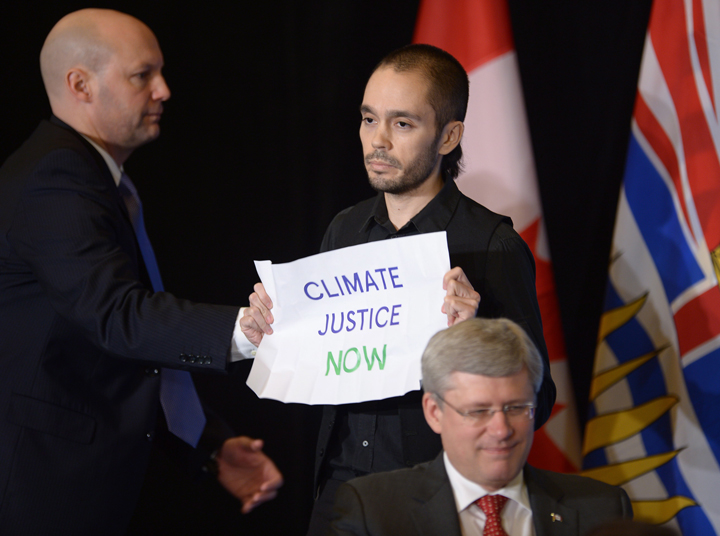 Protesters carry placards across stage as Stephen Harper speaks in ...